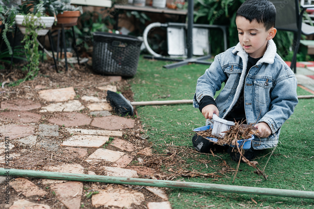 A child cleaning backyard in the morning. Little boy sweeping leaves ...