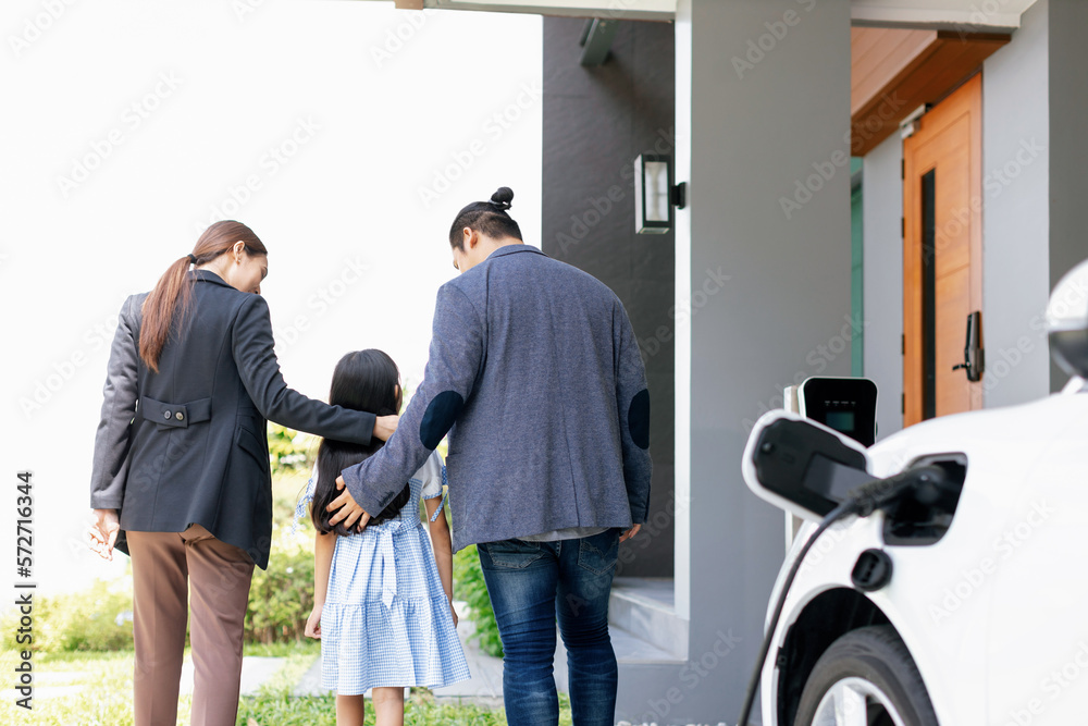 Progressive young parents and daughter with electric vehicle and home ...