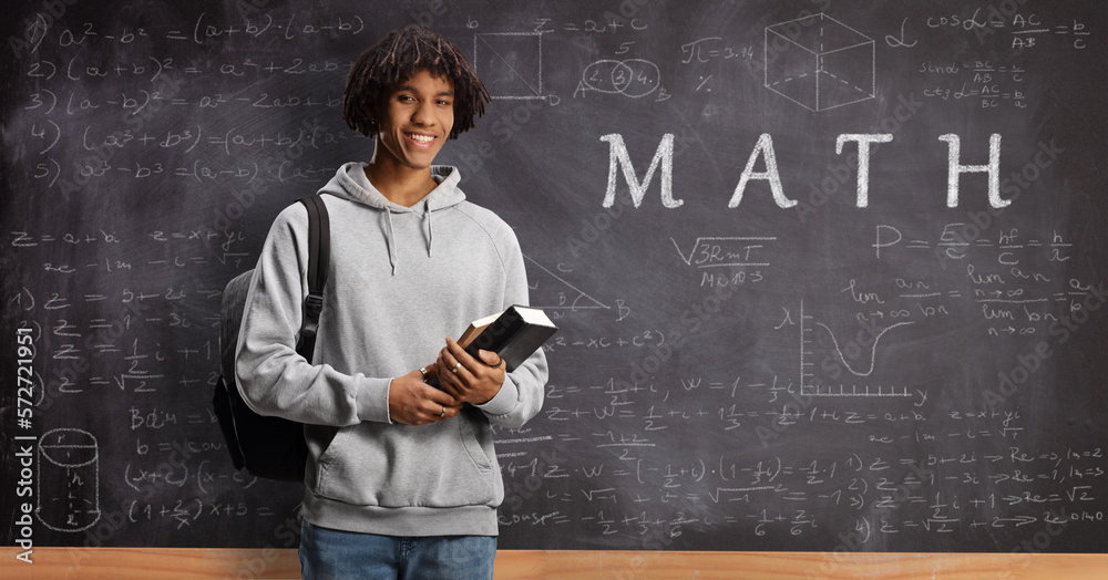 African american male student holding books in front of a blackboard ...