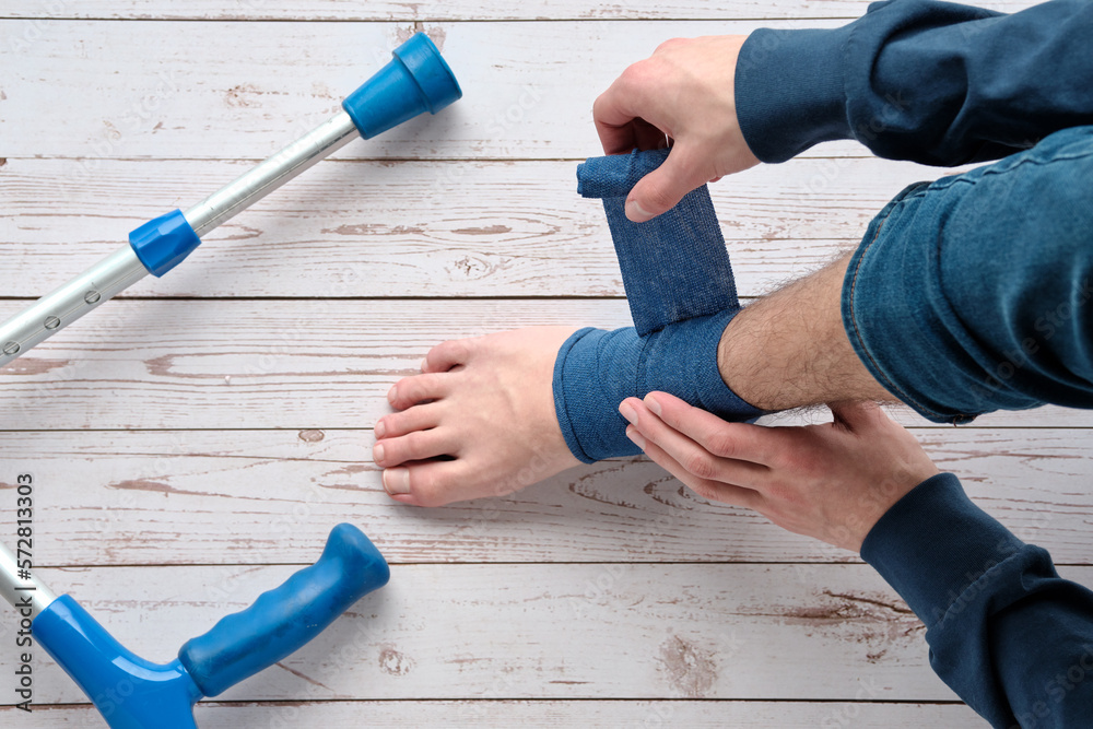 Teenage boy wrapping compression bandage around sprained ankle to ...