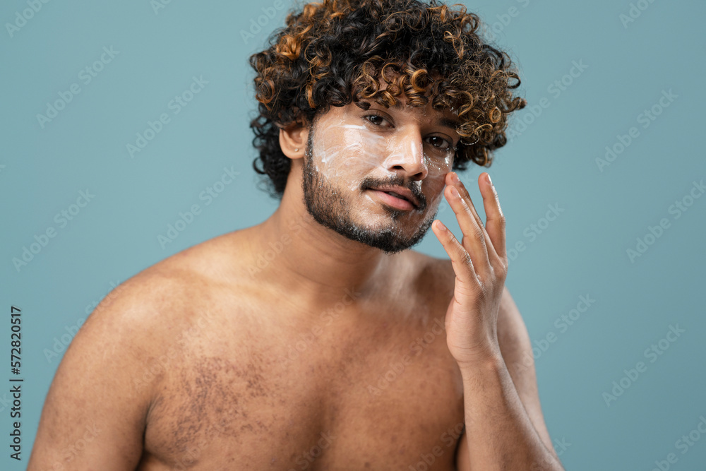 Foto de Shirtless Indian man applying moisturizer on face, isolated ...