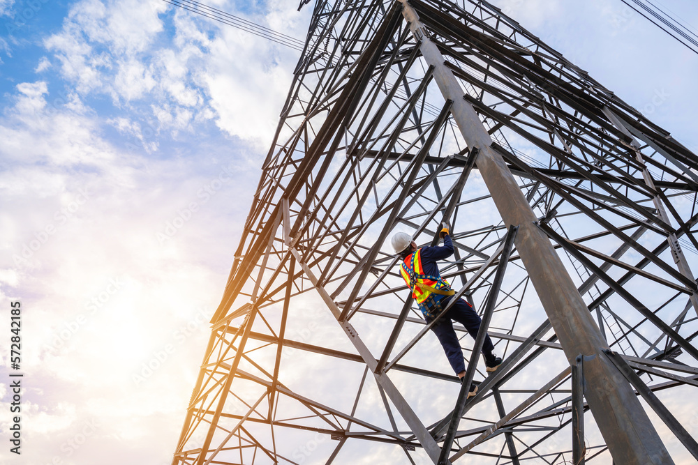 A workers wearing safety harnesses climb high-voltage pylons for inspection and maintenance at a ...