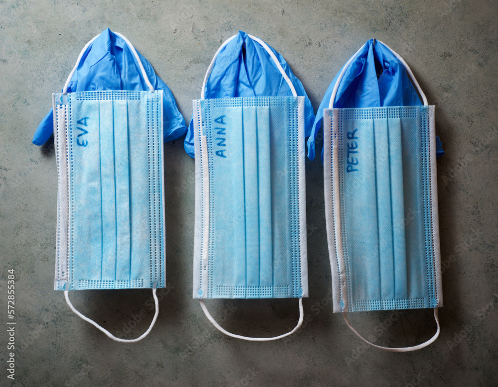 Surgical masks and gloves in a wall with the names of the users written ...