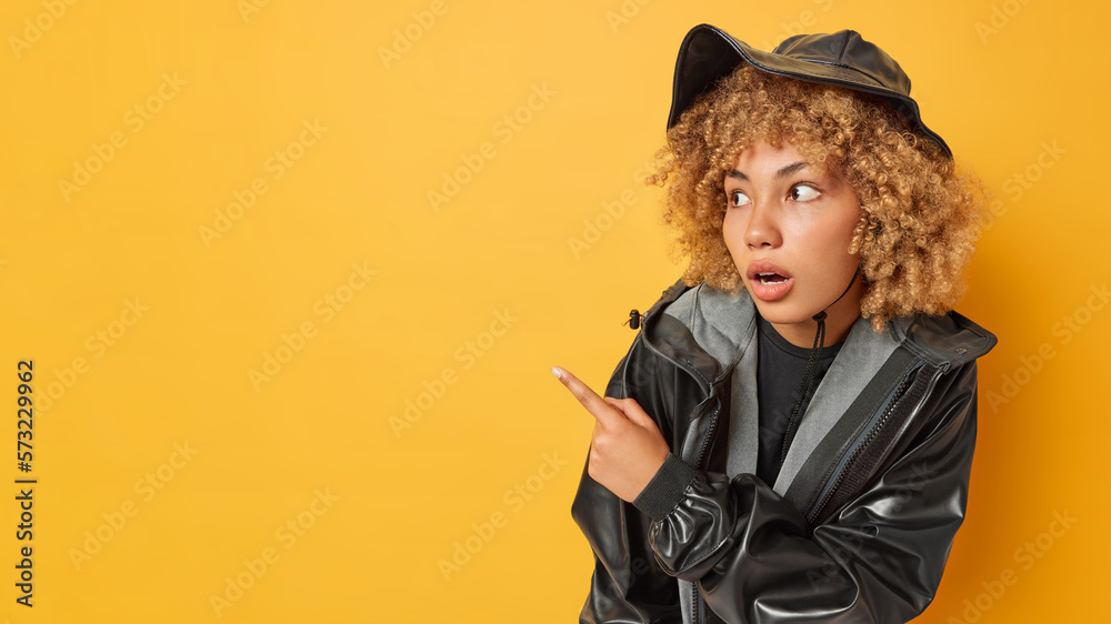 Stunned female model looks with scared shocked expression aside points ...