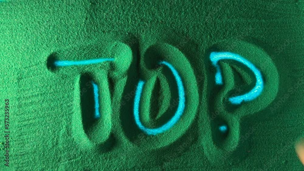 Hand drawing the Word Top in the Green Sand. Male hand writes the word ...