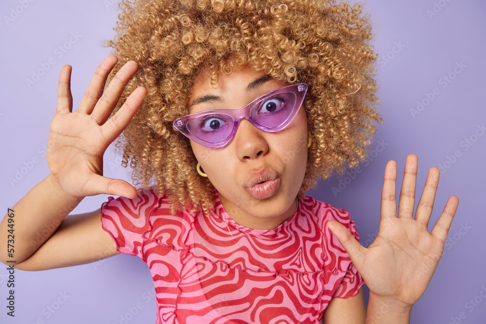 Portrait of surprised curly haired adult woman keeps palms raised ...