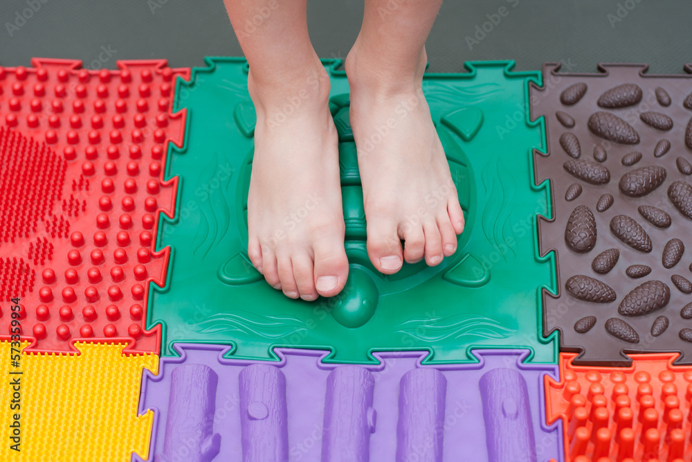 child does leg exercises on orthopedic massage mat at home. Puzzle mats ...