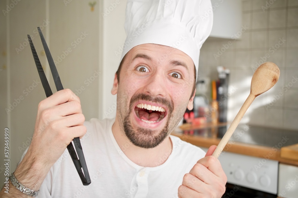 Happy chef in a professional kitchen, holding various cooking utensils ...