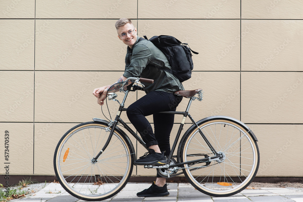 Young handsome man with bike over beige wall background in a city ...