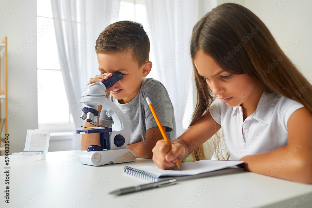 Two school kids use microscope and look at something at magnification ...