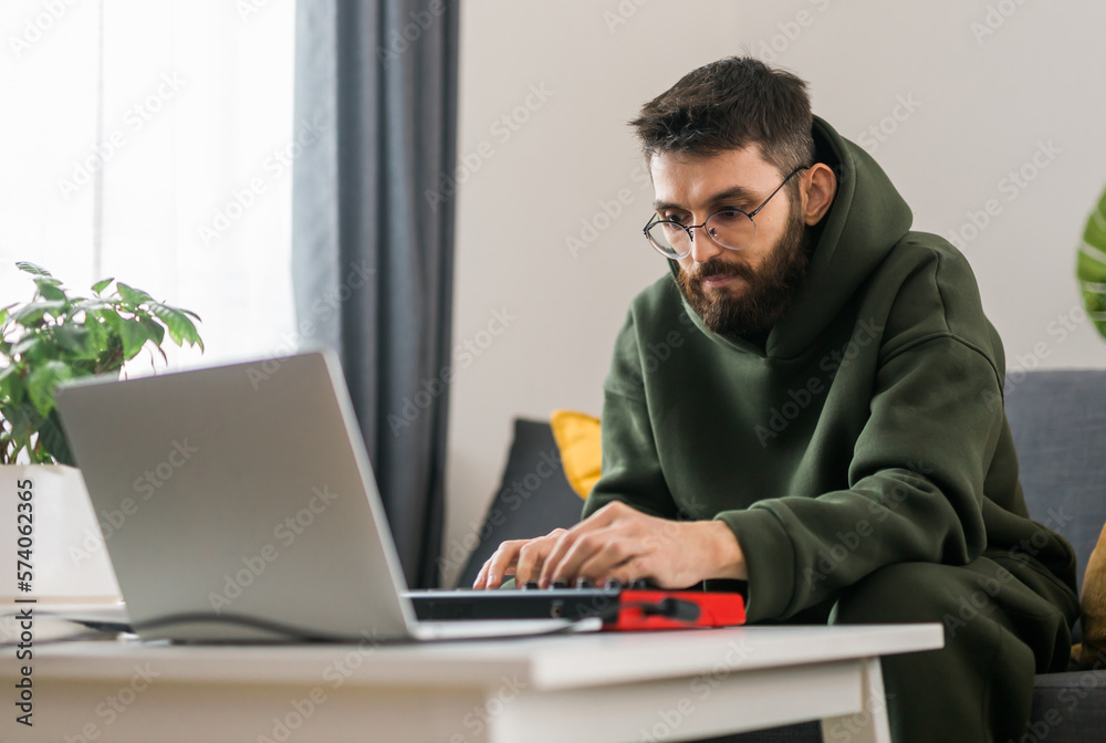 Man Recording Electronic Music Track With Portable Midi Keyboard On Laptop Computer In Home