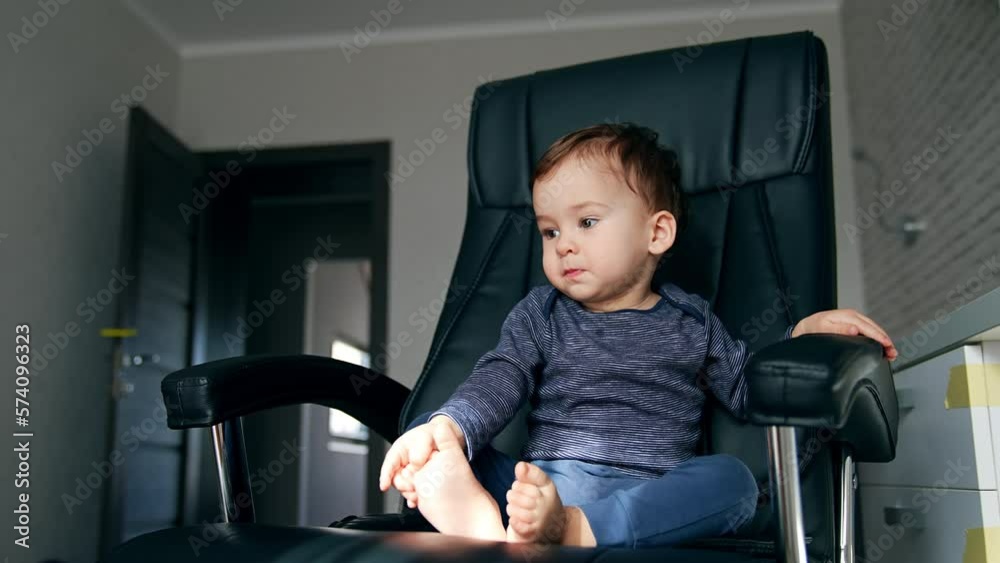 Pretty happy toddler sitting in a black office chair. Beautiful child ...