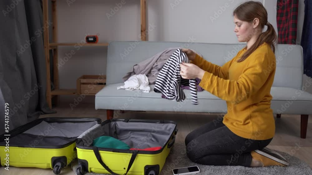 Young woman traveler sitting on the floor packing her suitcase, to do ...
