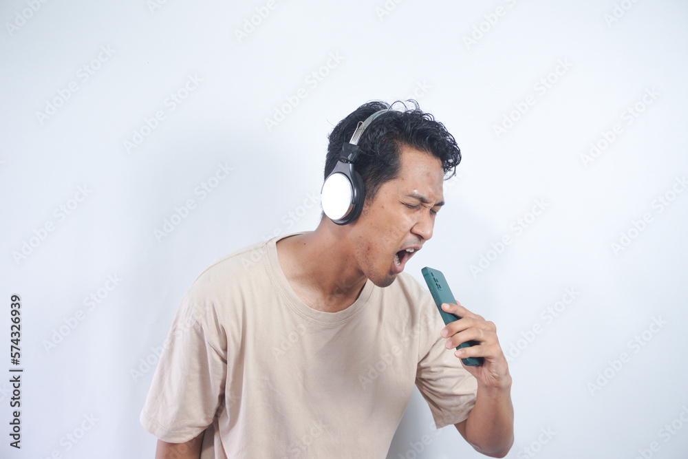 Energized man sings to music, moves actively, wears headphones and ...