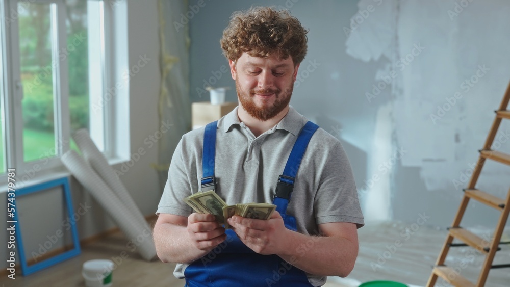 Repairman worker in blue overalls is counting money and smiling ...