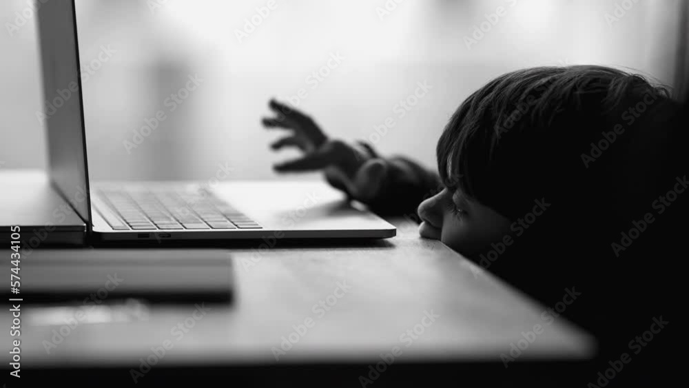 One bored little boy leaning on table and using computer laptop feeling ...