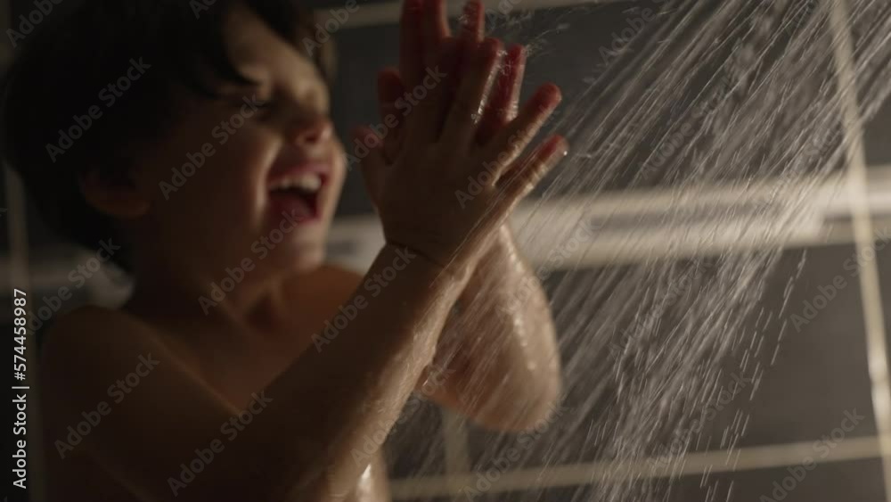 Washing happy child with shower head in slow motion. One small boy ...