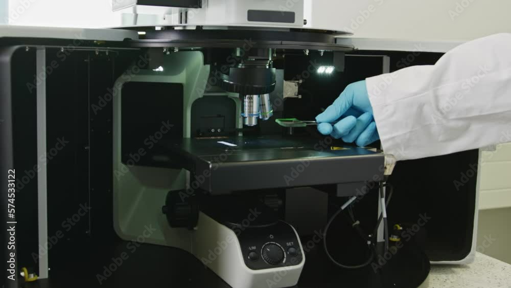 A slide is placed under the lens of a big microscope, which closes up ...