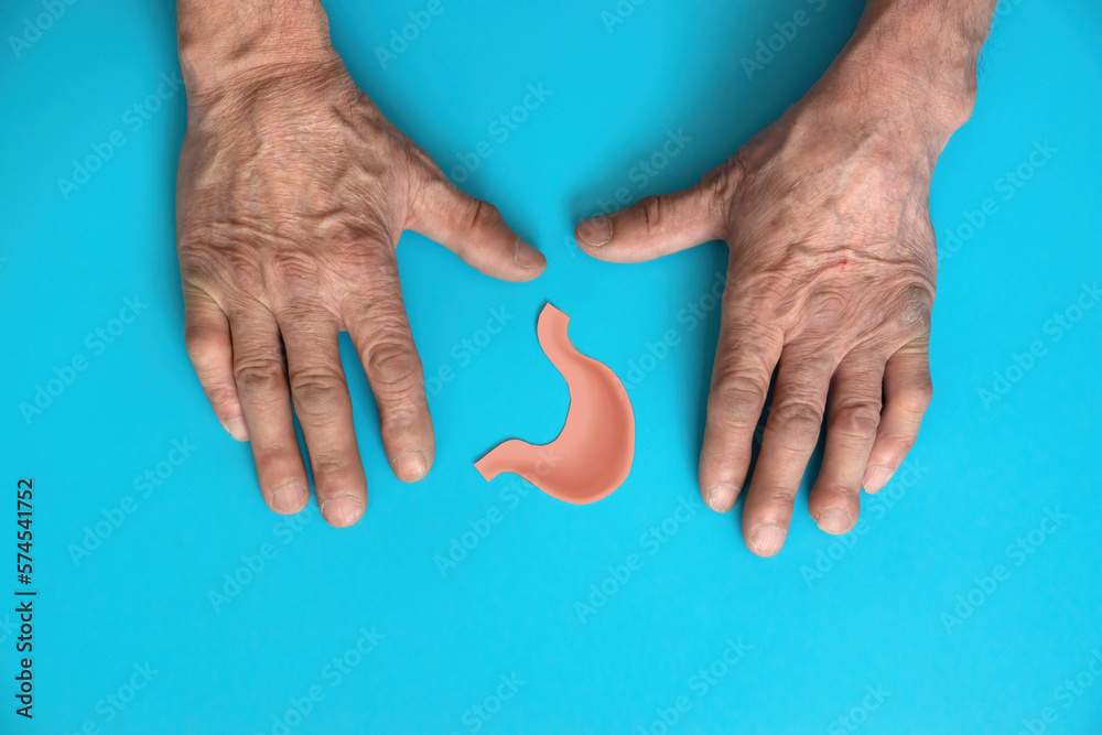 hands of an old man symbol organ stomach cut out of paper on a blue ...