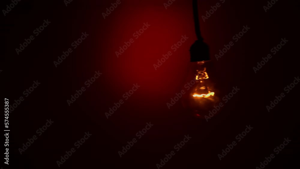 Light bulb staggers on a red background in the dark. Slow turning on ...