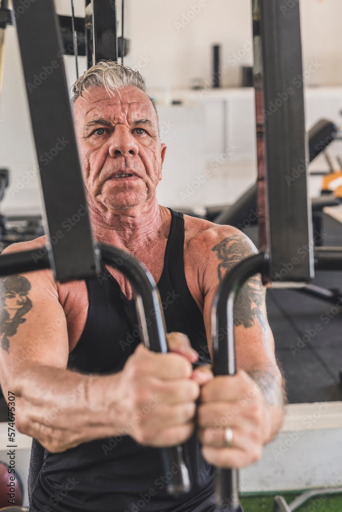 A rugged and tattooed older german man does a set of chest flyes on the ...