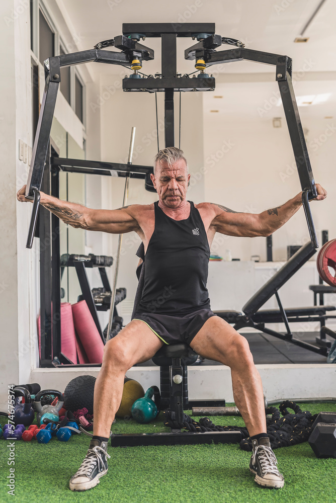 A rugged and tattooed older german man does a set of chest flyes on the ...