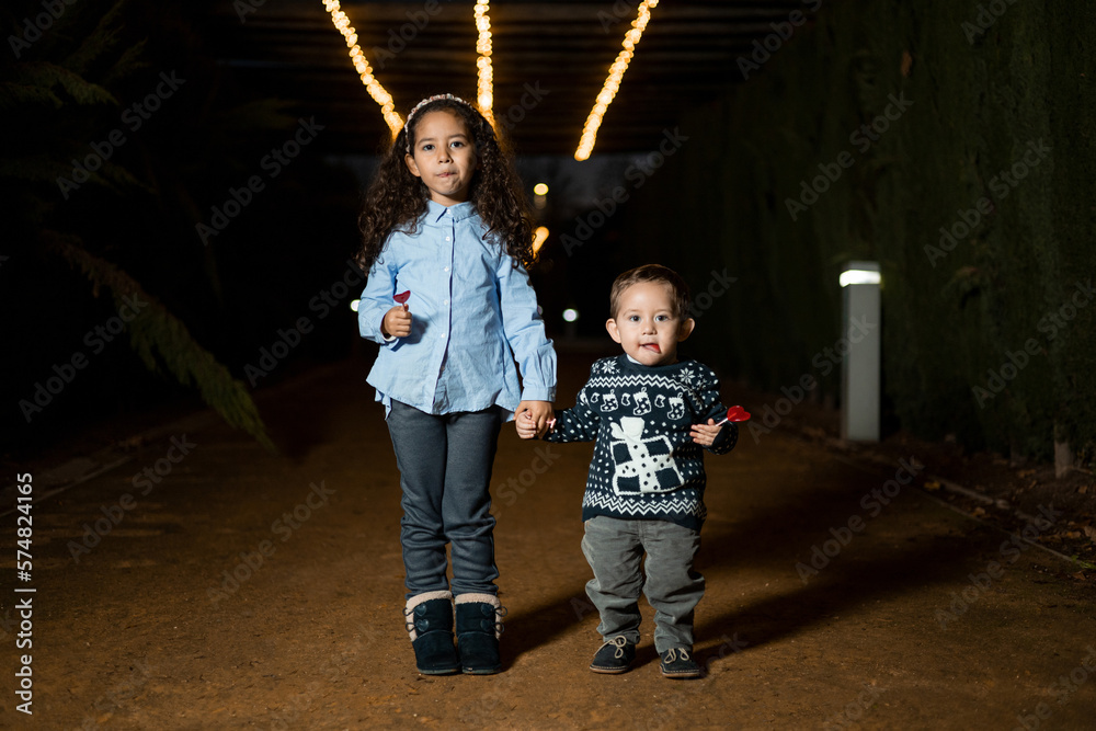 Two dark-skinned children posing outdoors at night holding hands while ...