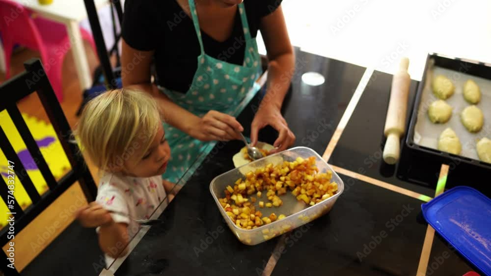 Little girl tries the filling with a spoon next to her mother making ...