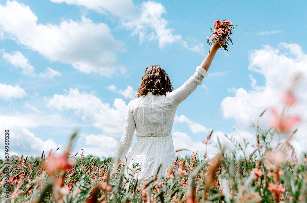 Back view of woman in white dress holding up a flower bouquet in a ...