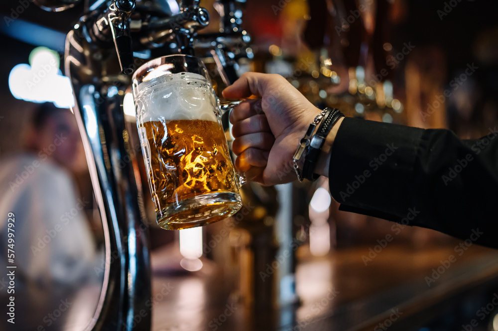 man bartender hand at beer tap pouring a draught beer in glass serving ...