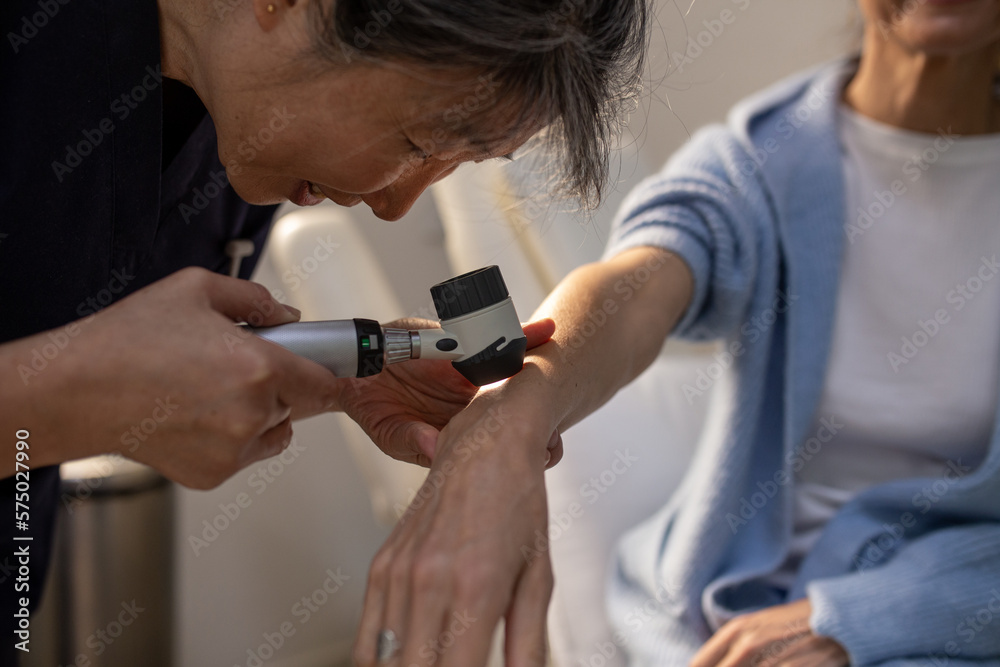 Female health worker using a dermatoscope to check the arm skin of a ...