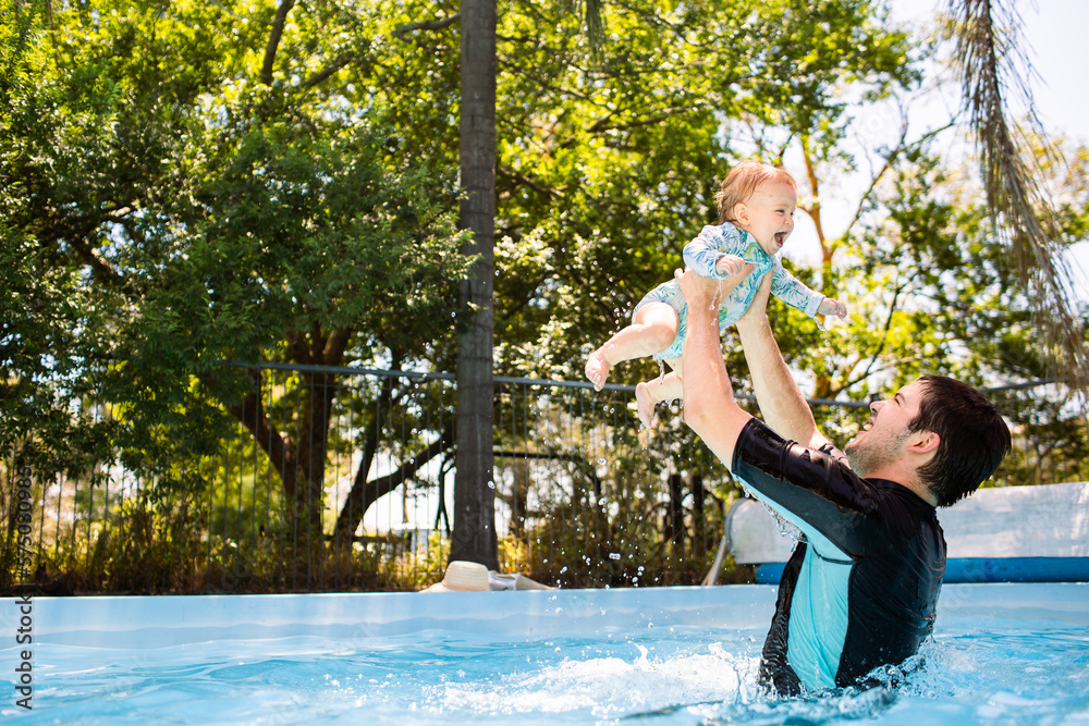 Father playing with baby in swimming pool dad lifting child high into ...