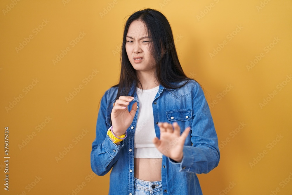Young asian woman standing over yellow background disgusted expression ...