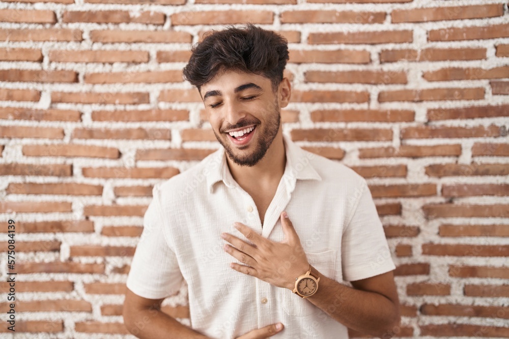 Arab man with beard standing over bricks wall background smiling and ...