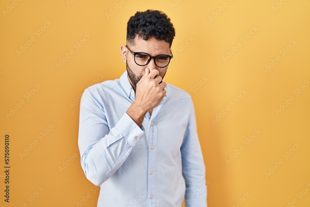 Hispanic man with beard standing over yellow background smelling ...