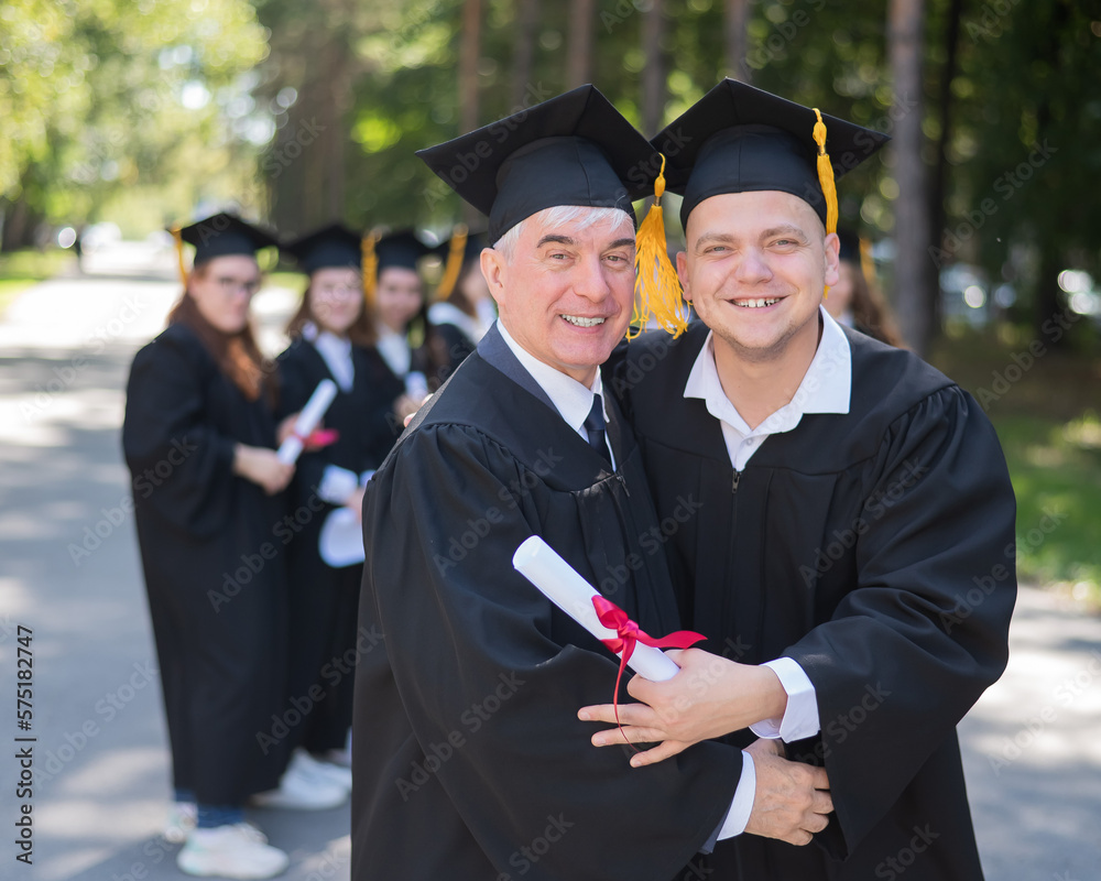 A group of graduates in robes outdoors. An elderly man and a young guy ...
