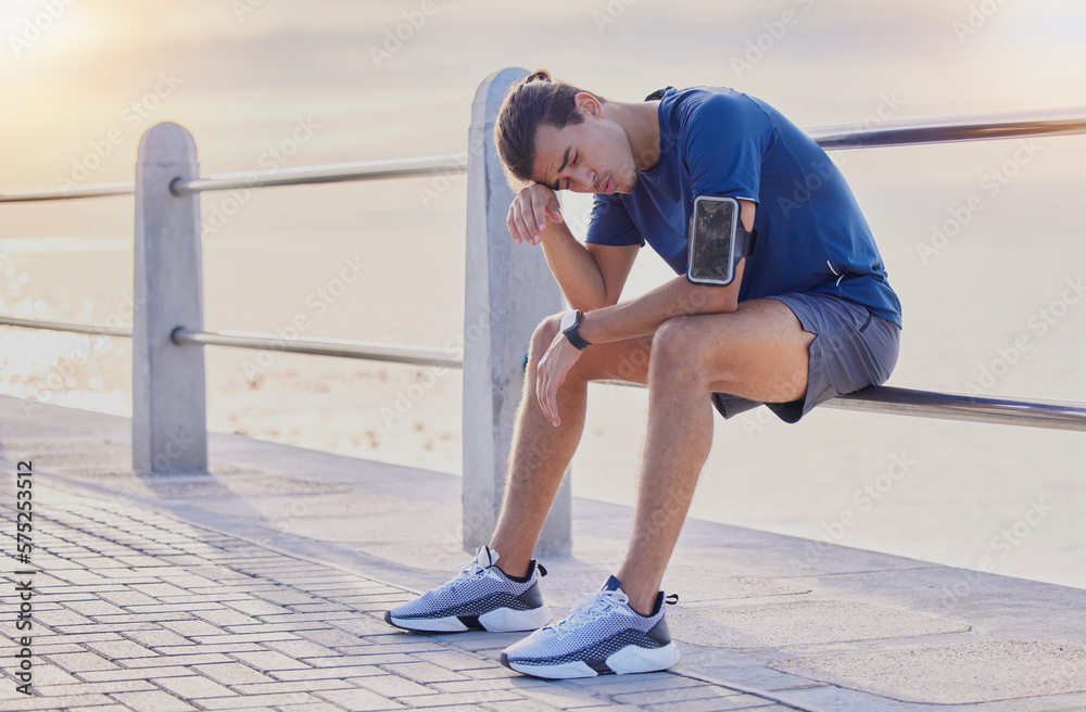 Tired runner man, sitting and beach for workout, health and exercise ...