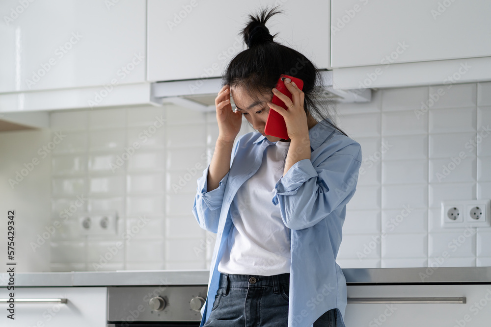 Sad depressed young Asian woman standing at home talking phone, hearing ...