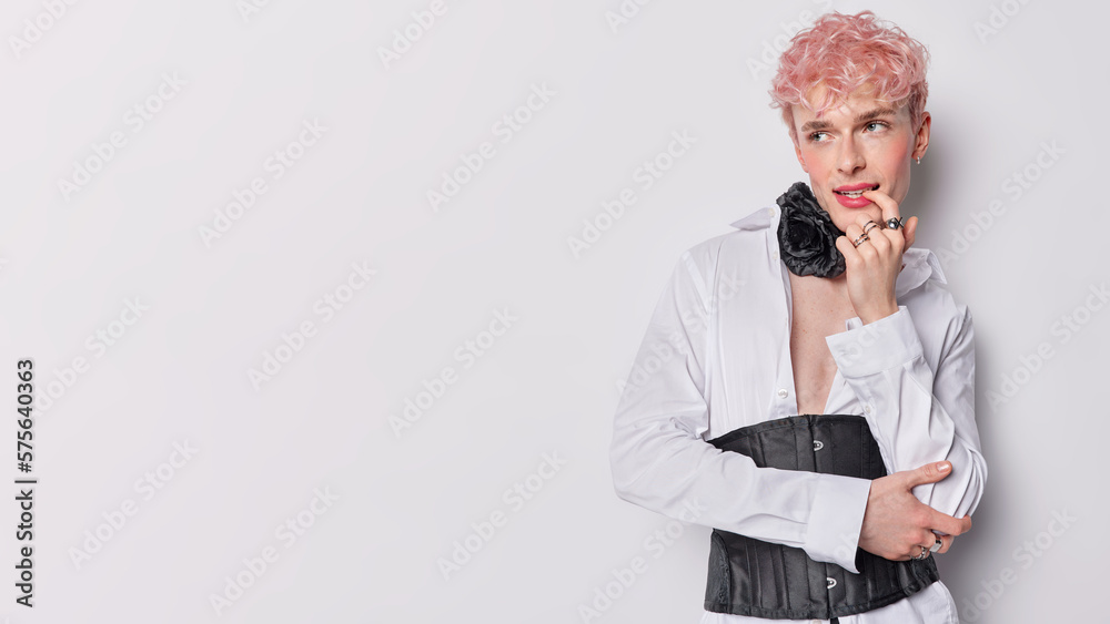 Androgynous man with pensive expression bites finger focused aside ...