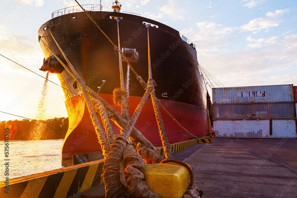 A cargo ship moored to the mooring bollard of the seaport with ropes ...