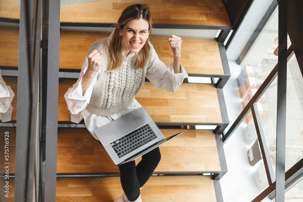 Girl rejoices in winning having raised her hands up sitting on stairs ...