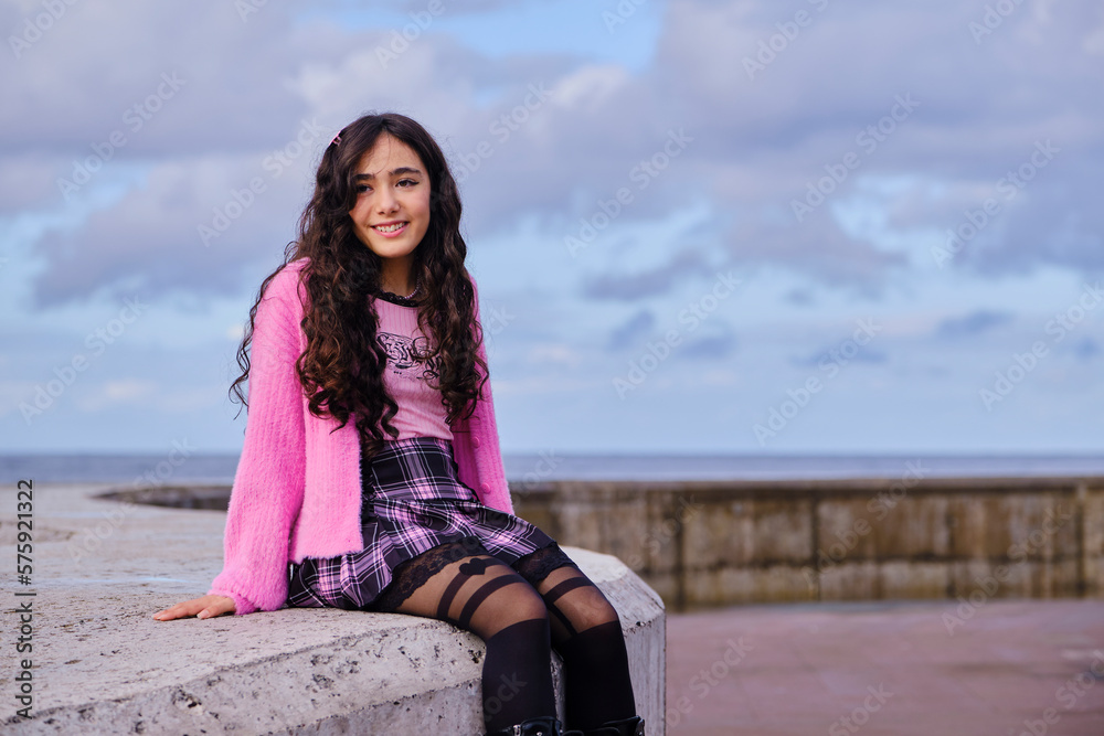 Gothic looking teenage girl posing sitting on a wall in front of the ...
