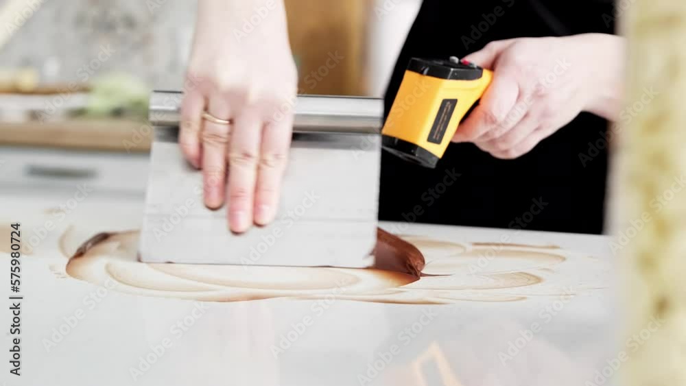 Pastry chef at work tempering chocolate using spatula and pyrometer on ...