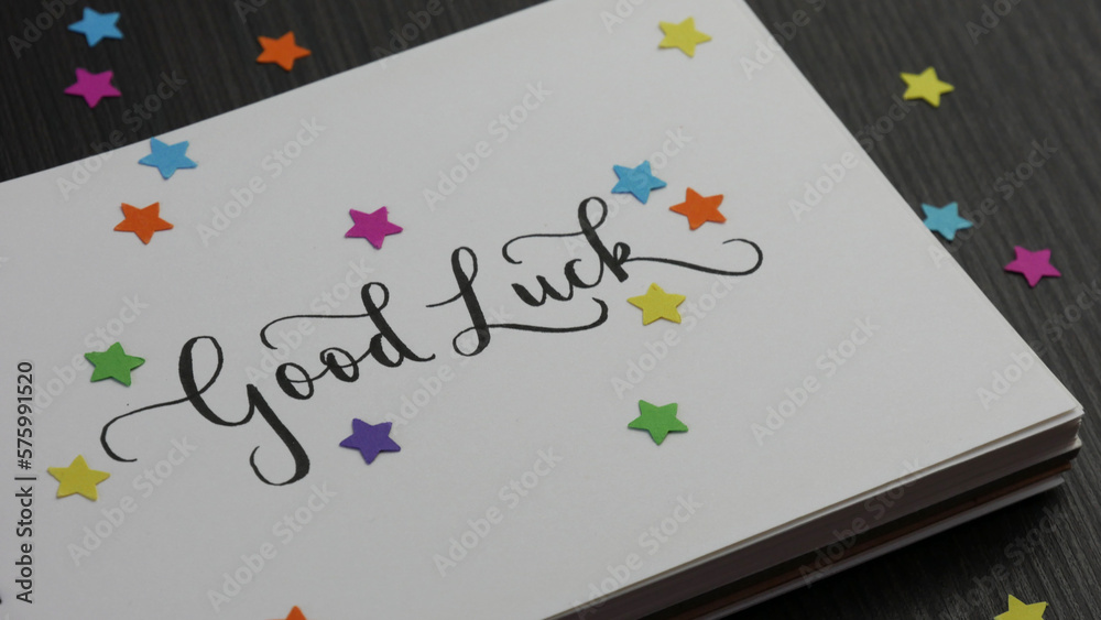 GOOD LUCK lettering in notebook with colorful stars on black wooden ...
