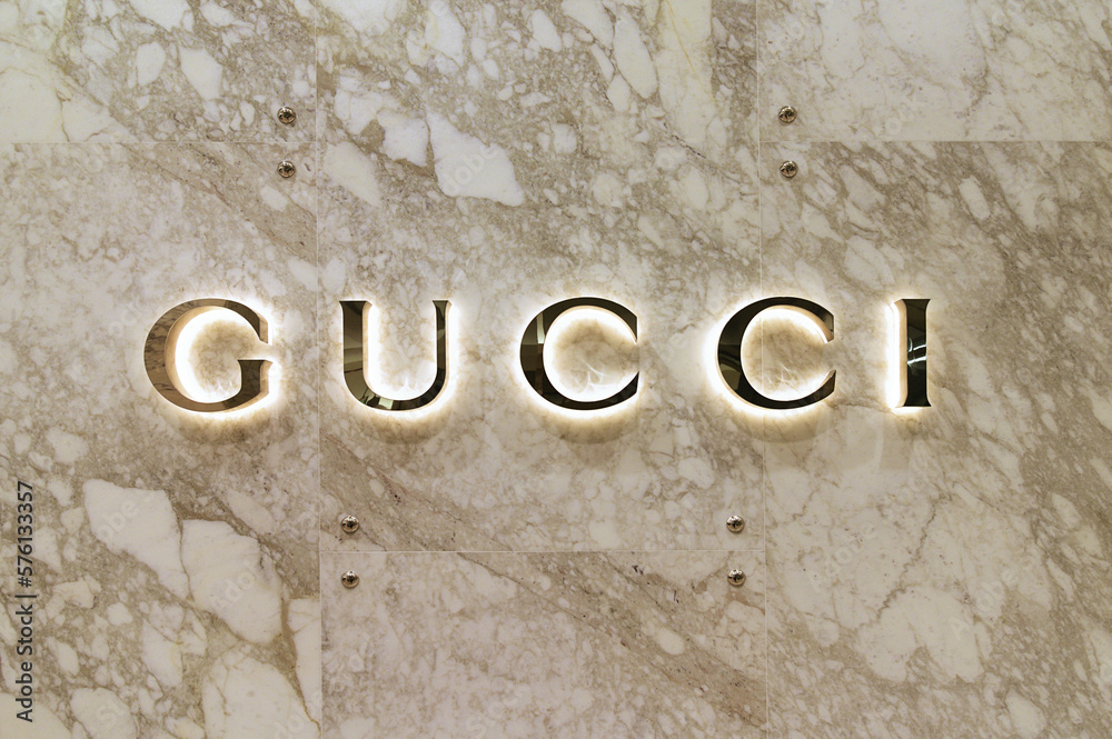 Backlit gold Gucci brand logo on tan marble wall Stock Photo | Adobe Stock