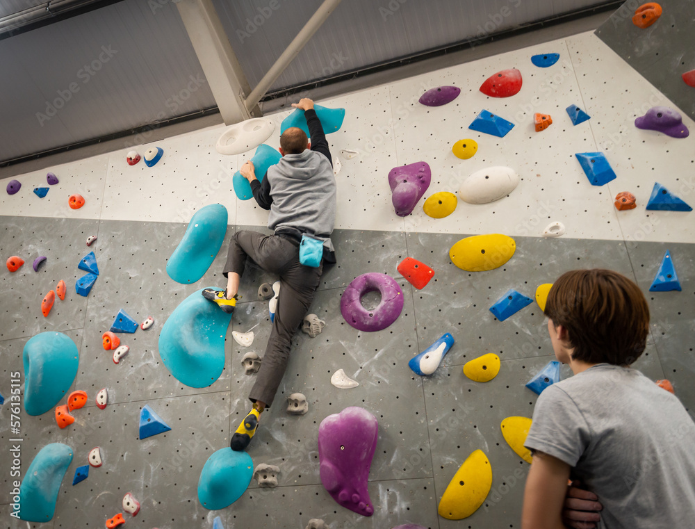 Male climber traversing indoor climbing wall using holds and grips of ...