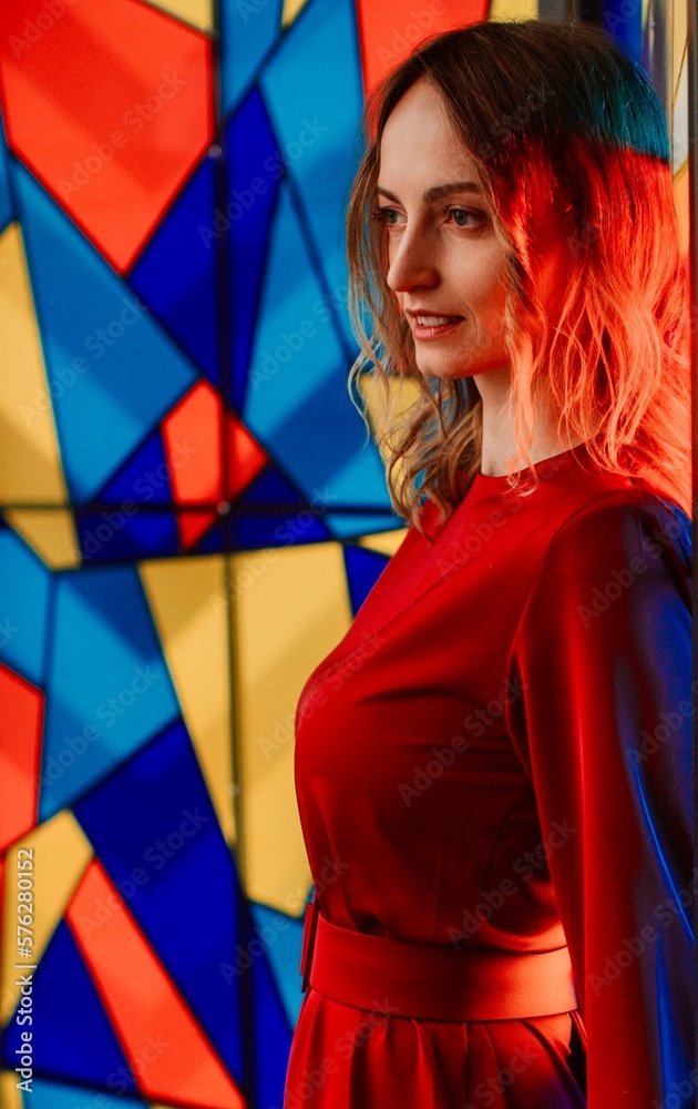 Beautiful woman in red dress in front of colorful stained glass window ...