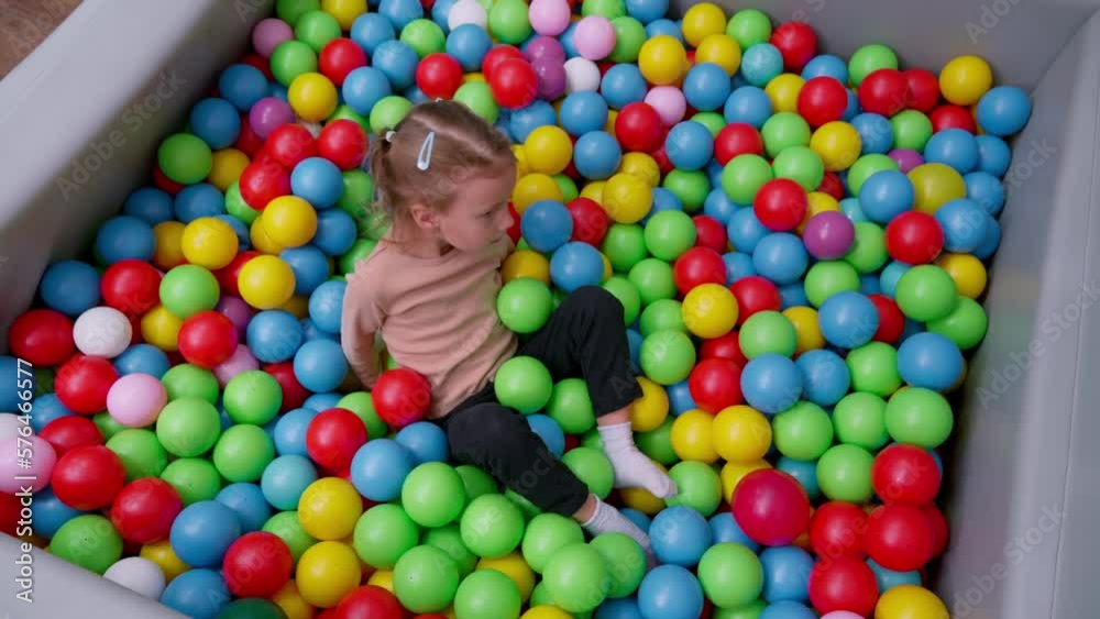 Cute little girl playing on multi coloured plastic balls in big dry ...