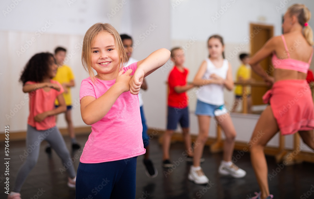 Portrait of cheerful preteen girl practicing dance movements with group ...