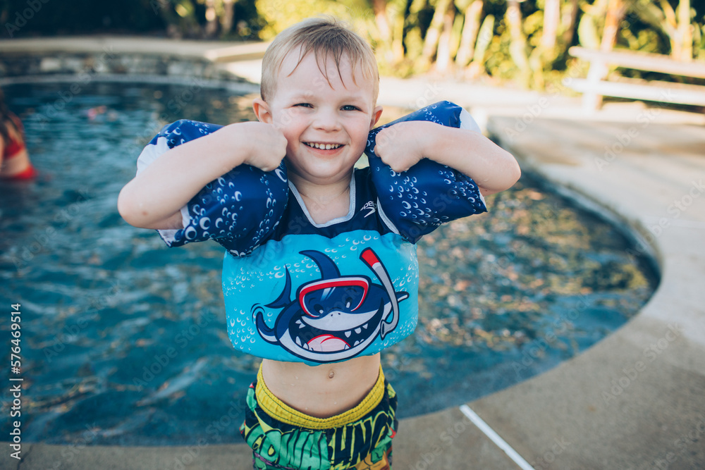 little boy wearing a lifejacket floaties making muscles in front of a ...